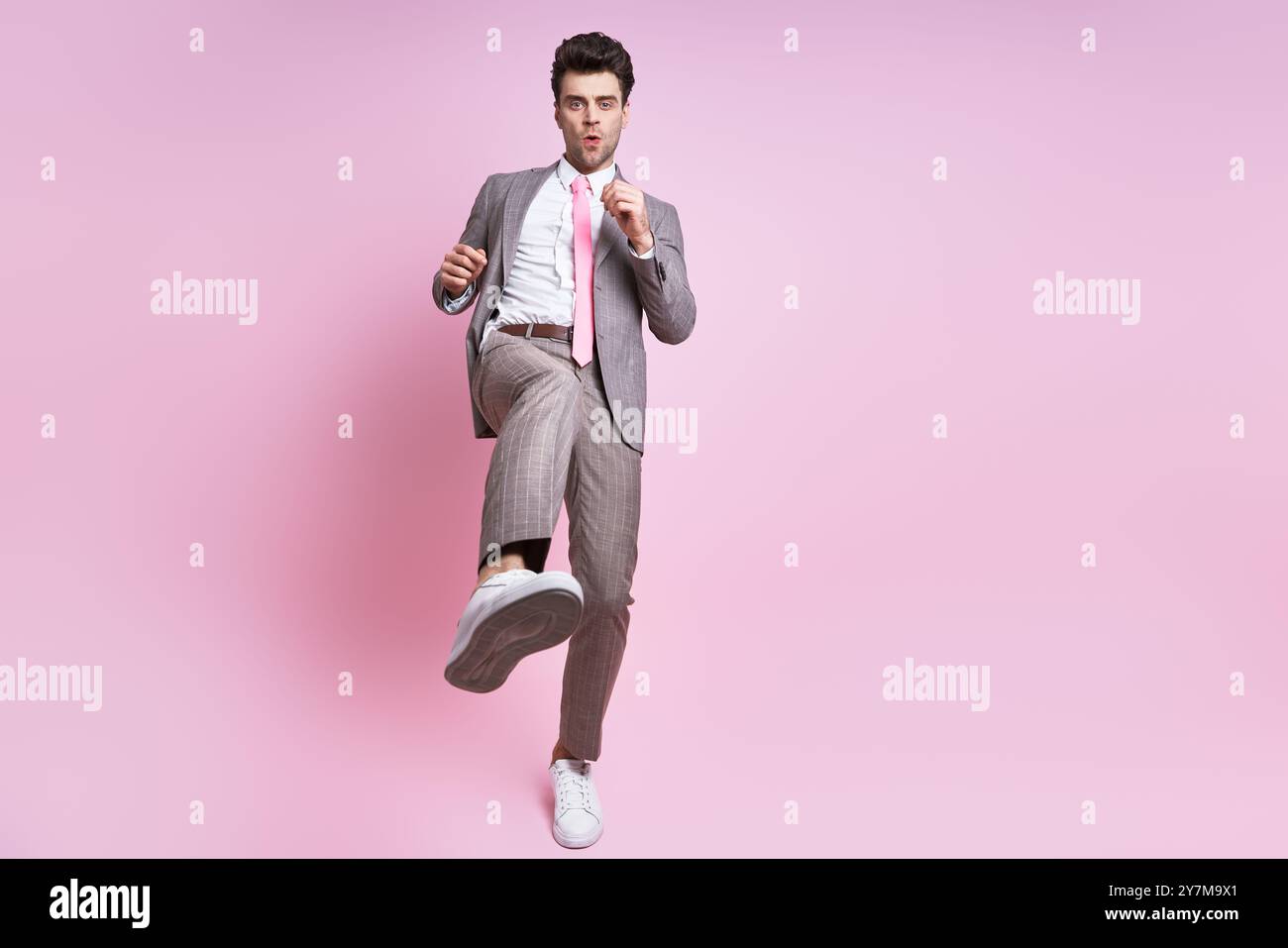 Furious young man in full suit throwing leg kick while standing against ...