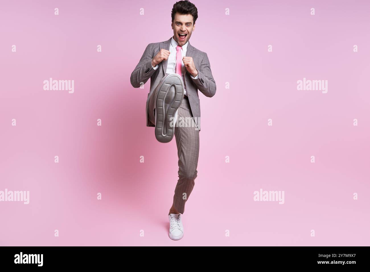Angry young man in full suit throwing leg kick while standing against ...