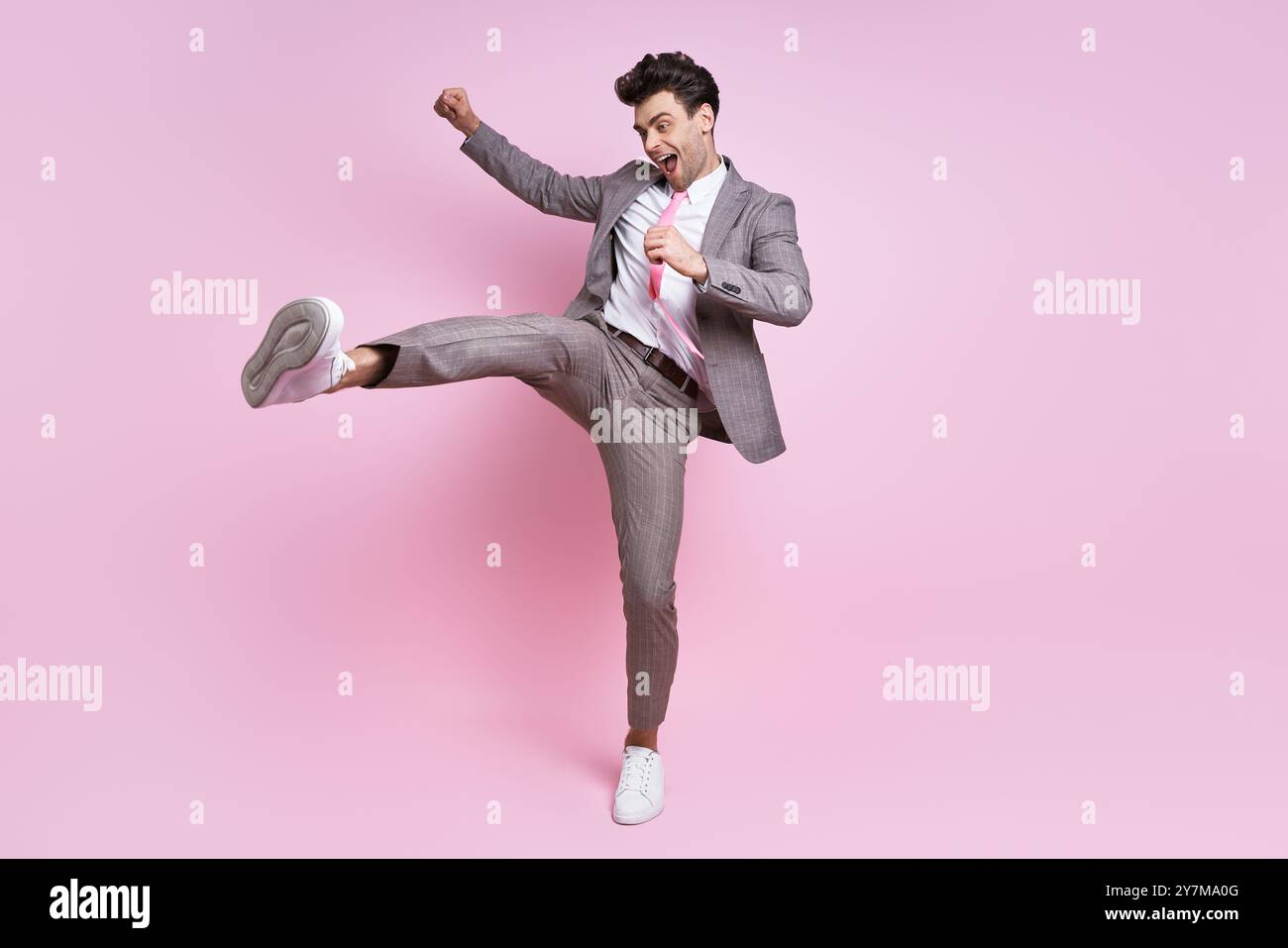 Excited young man in full suit throwing leg kick while standing against ...