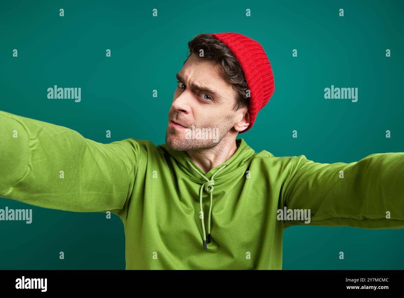 Angry young man stretching out hands while standing against green ...