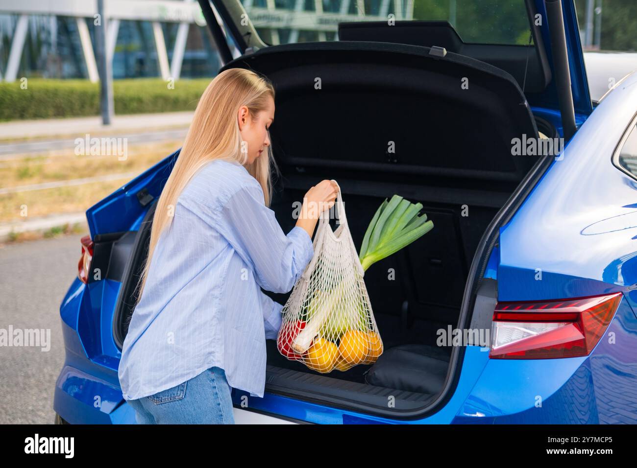 Blonde woman with long hair loading fresh vegetables into the trunk of ...