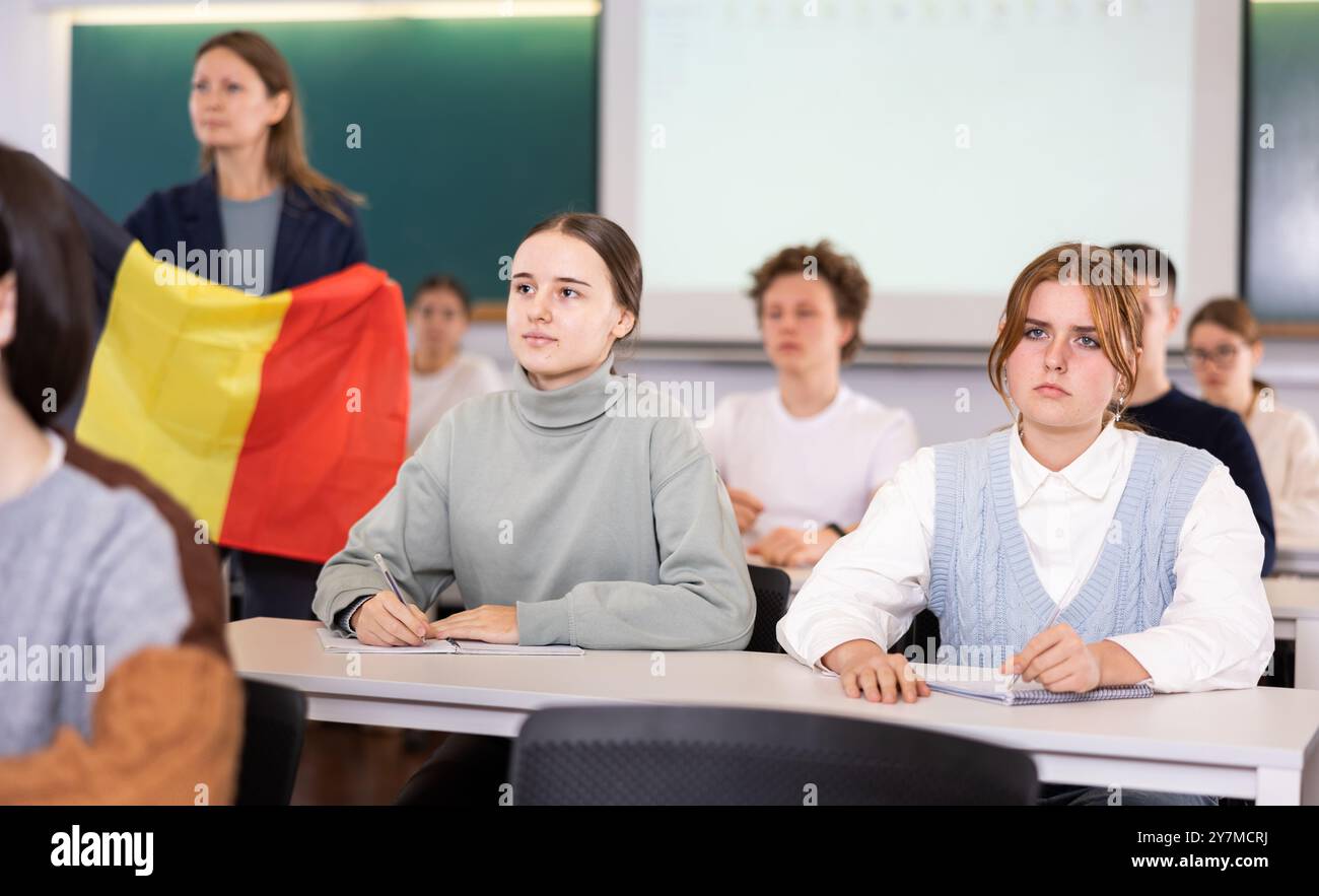 Teenage students sitting in class and listening carefully to female ...