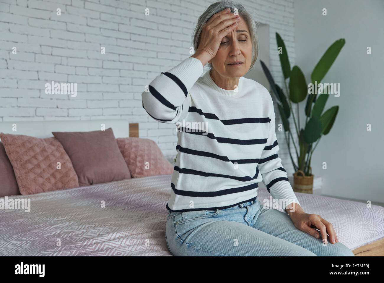 Frustrated senior woman touching forehead while sitting on the bed at ...