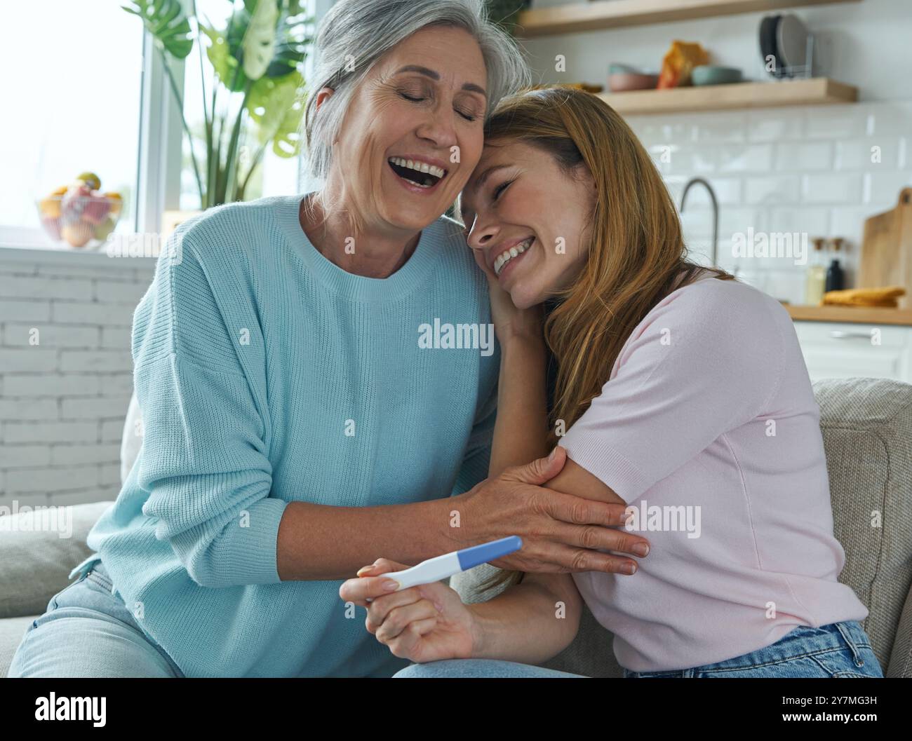 Happy young woman holding pregnancy test and embracing her mother while ...