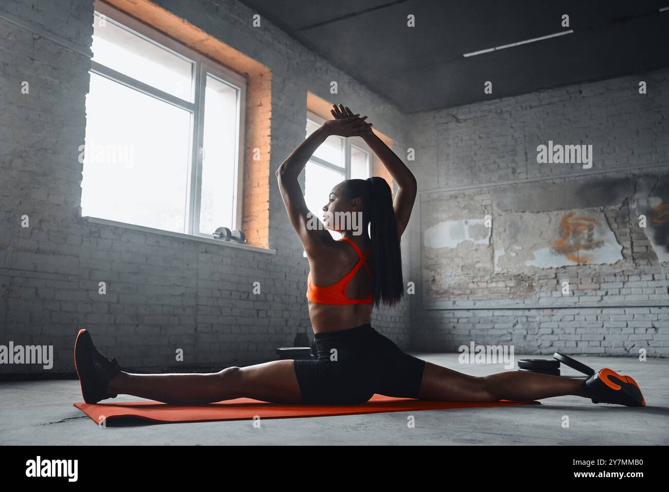 Rear view of beautiful young African woman stretching on splits in gym ...