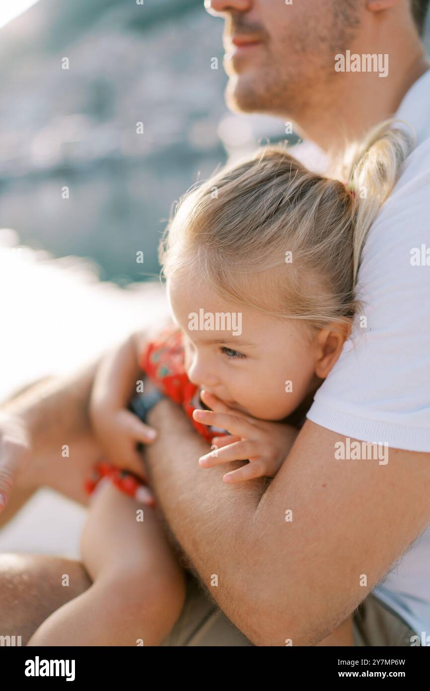 Little smiling girl sits on her dad lap, leaning on his hand and ...