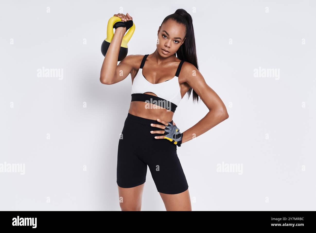 Beautiful young African woman exercising with kettlebell against white ...