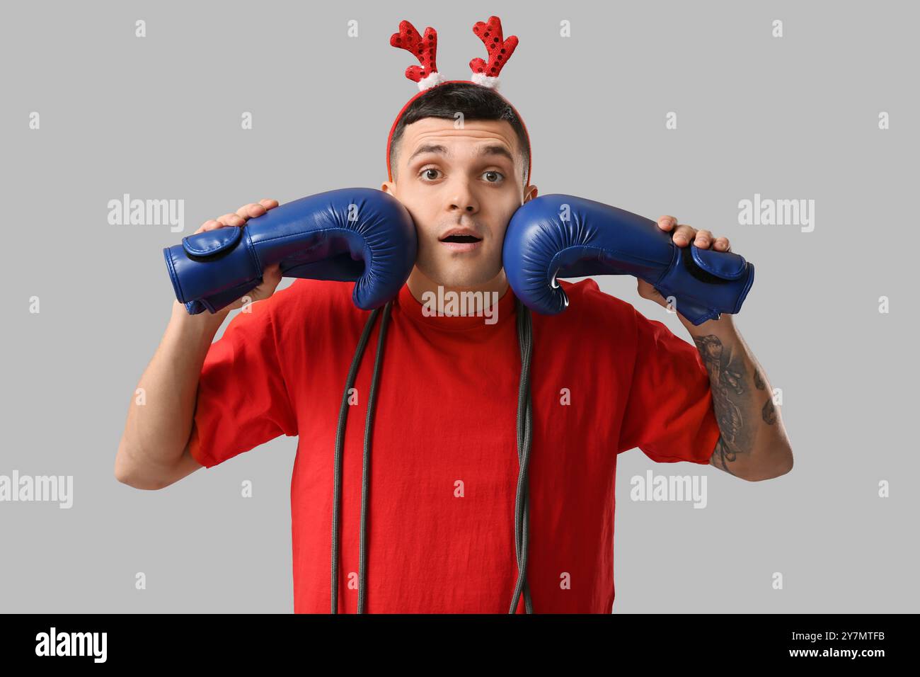 Young surprised man in reindeer horns with skipping rope and boxing ...
