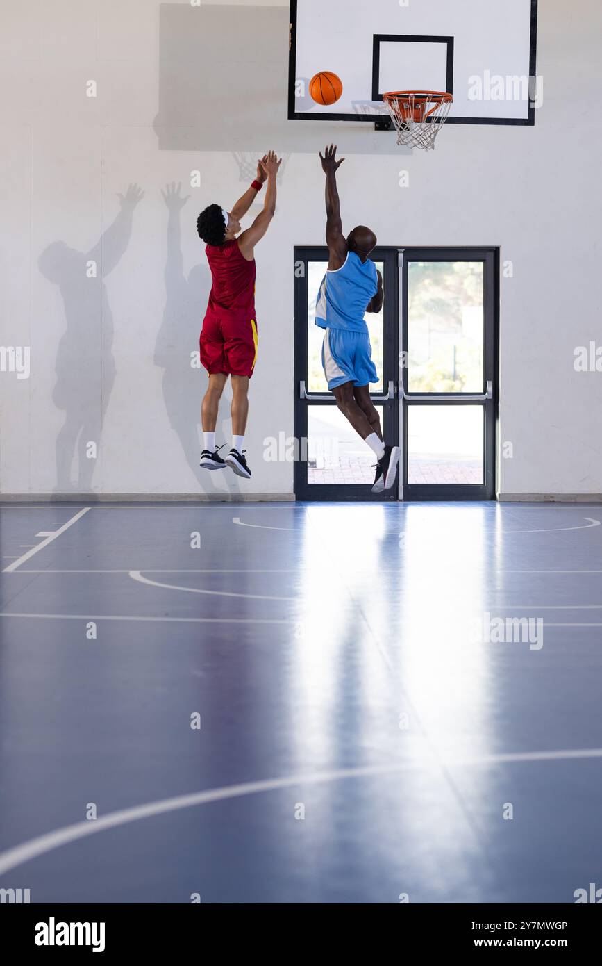 Playing basketball, two men jumping to shoot and block ball in indoor ...