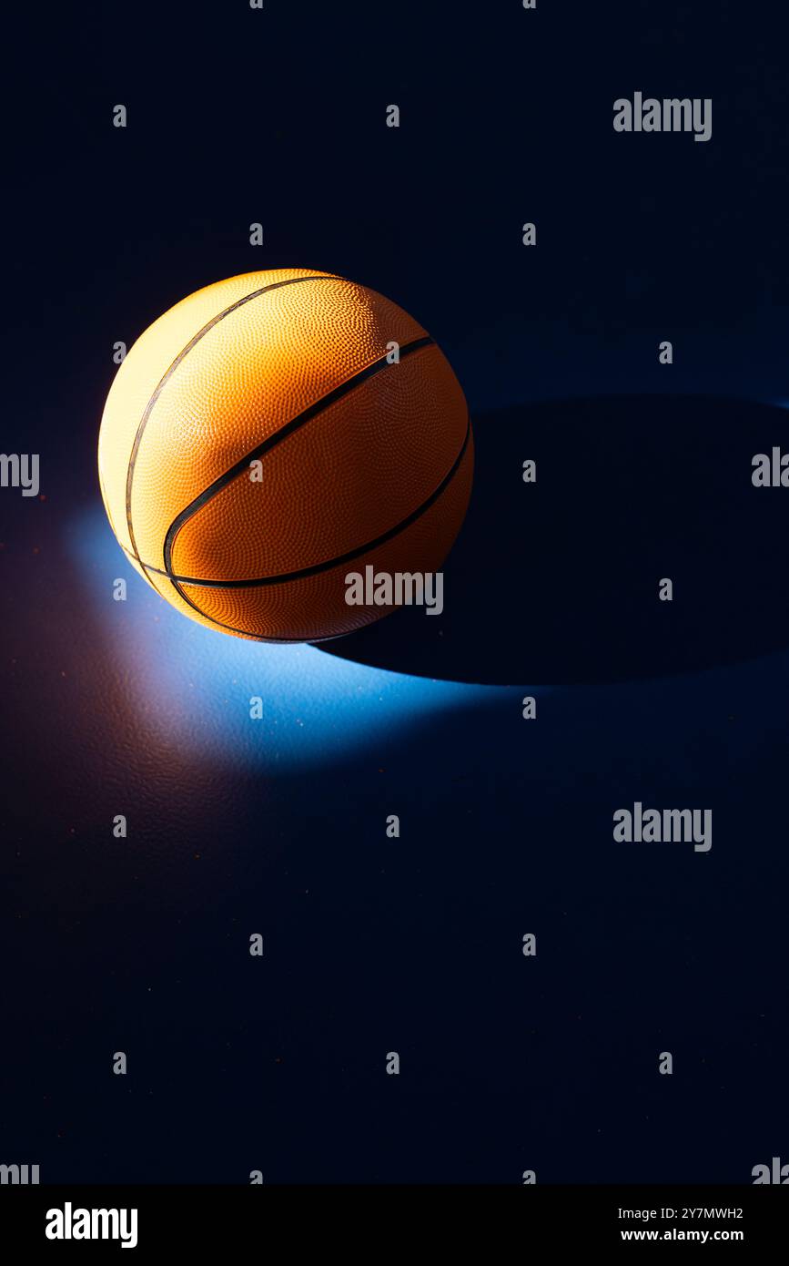 Basketball resting on court under spotlight, casting shadow on floor ...