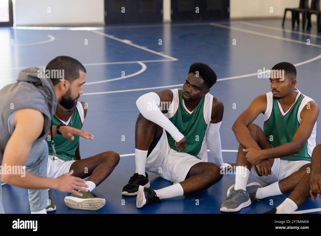 Basketball coach discussing strategy with players sitting on court ...