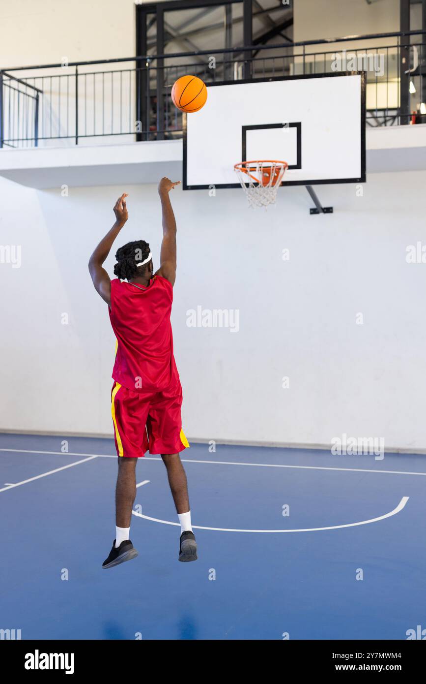 Playing basketball, athlete shooting ball towards hoop in indoor court ...