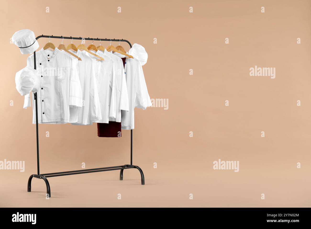 Different chef's uniforms on clothing rack against beige background ...