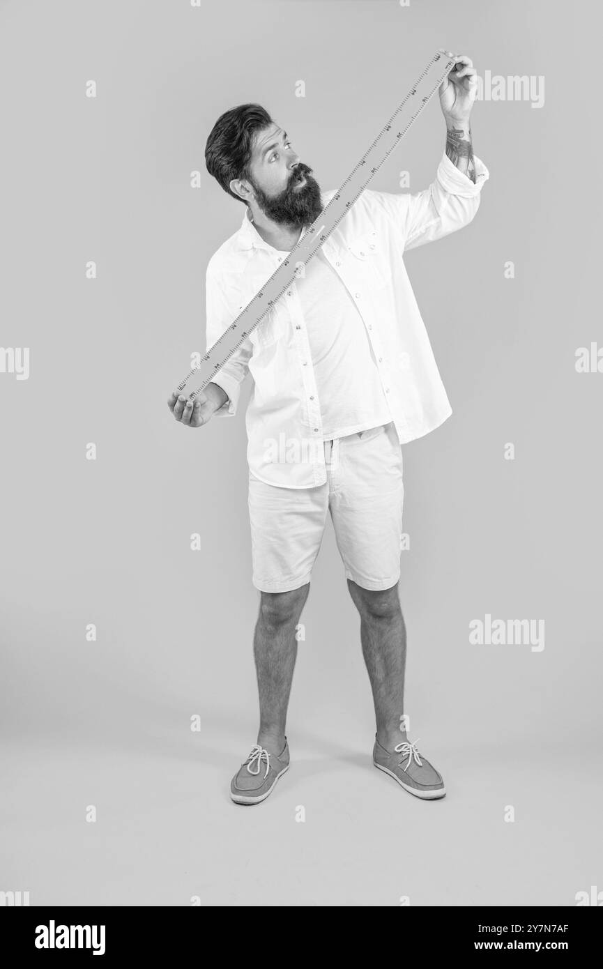 photo of surprised man hold school ruler isolated on yellow background ...