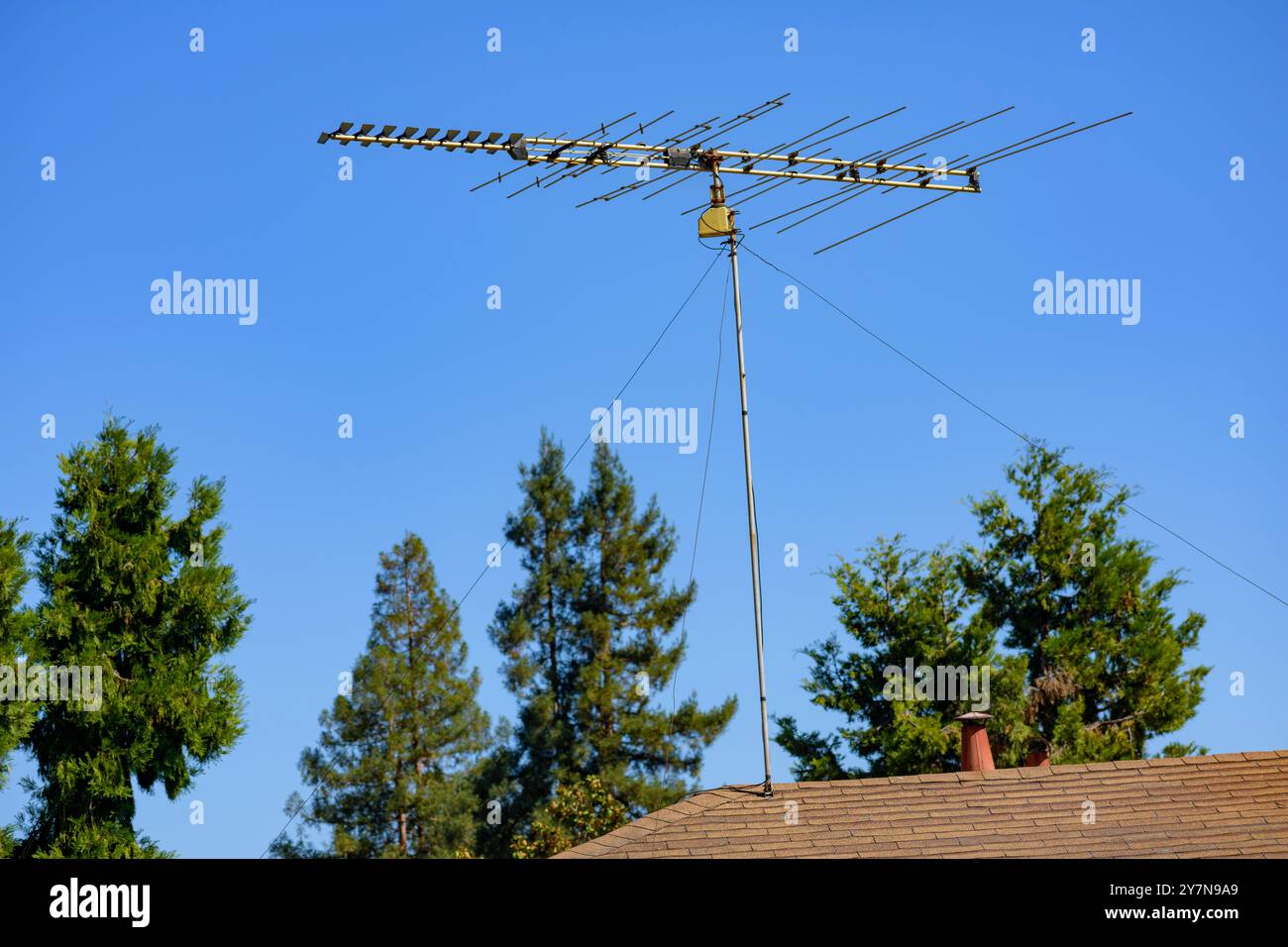 A rooftop-mounted outdoor TV antenna rises above a shingled roof of ...