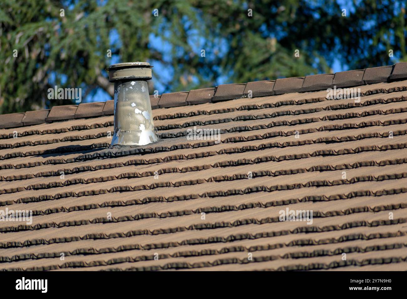A weathered metal roof vent with peeling paint is set on top of a brown ...