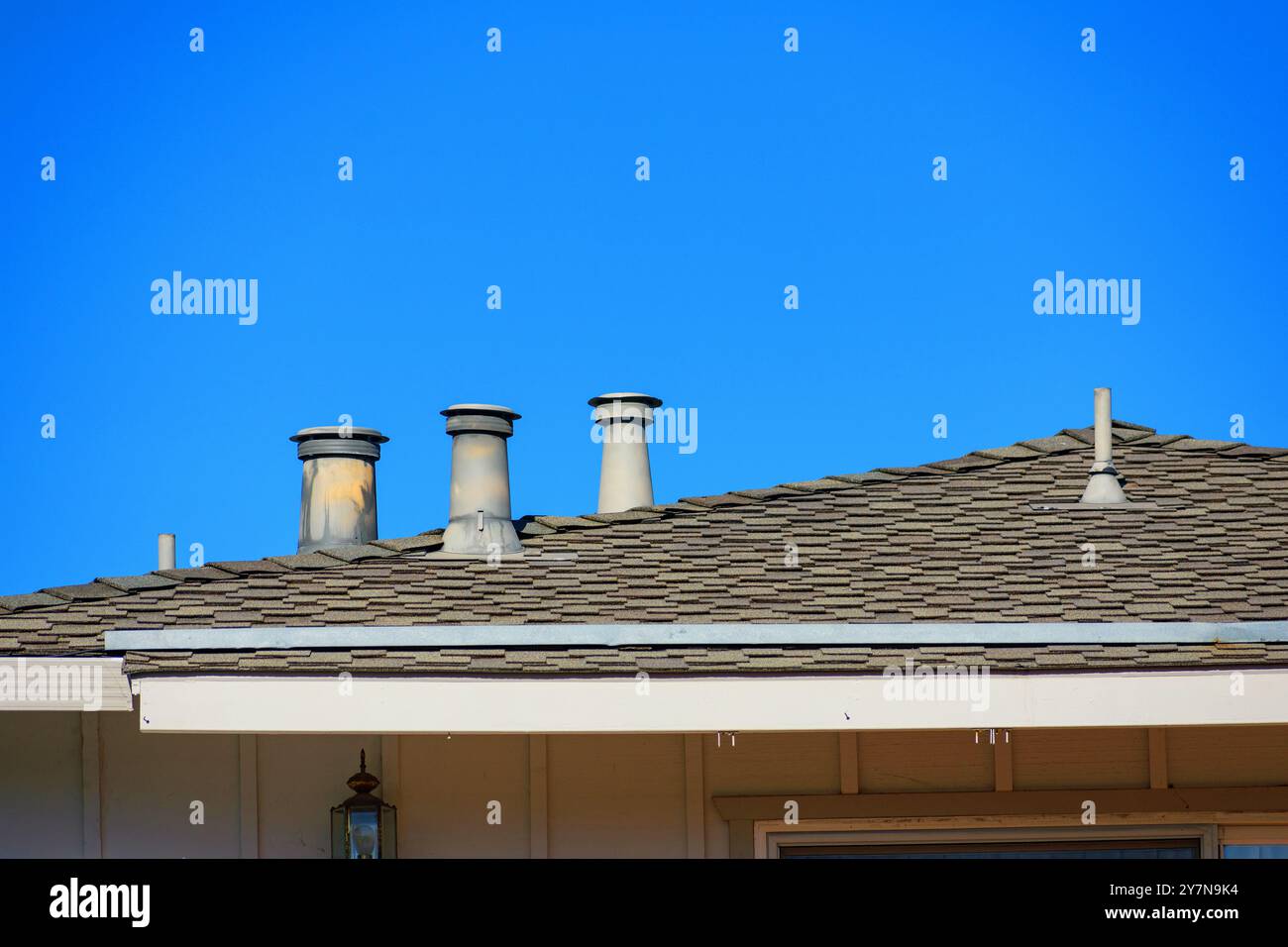Several rooftop vents rise from a shingled roof under a clear blue sky ...