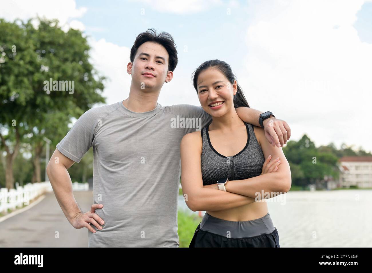 A lovely, active Asian couple in sportswear stands in a park, smiling ...