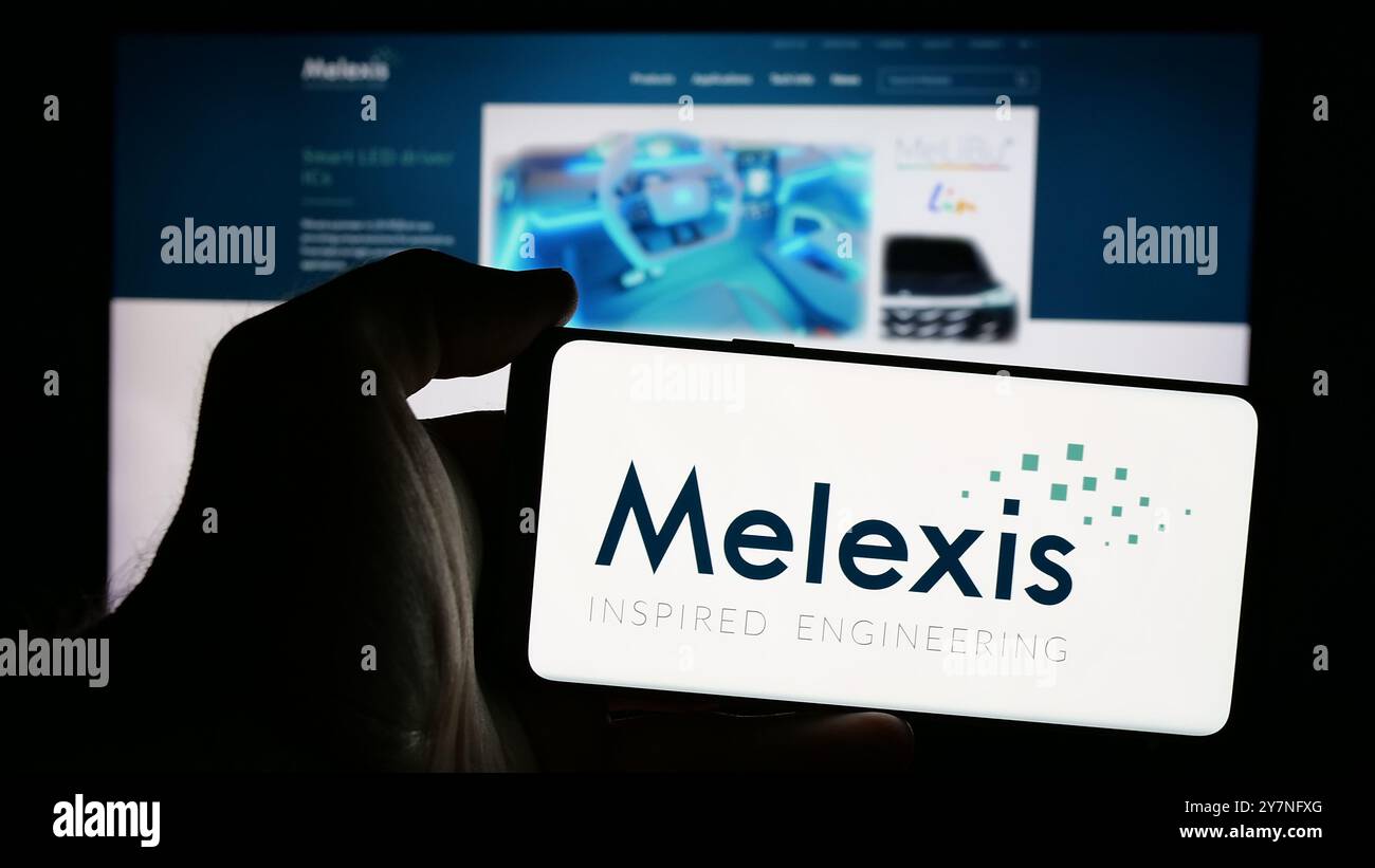 Person holding mobile phone with logo of Belgian semiconductor company Melexis N.V. on screen in ...