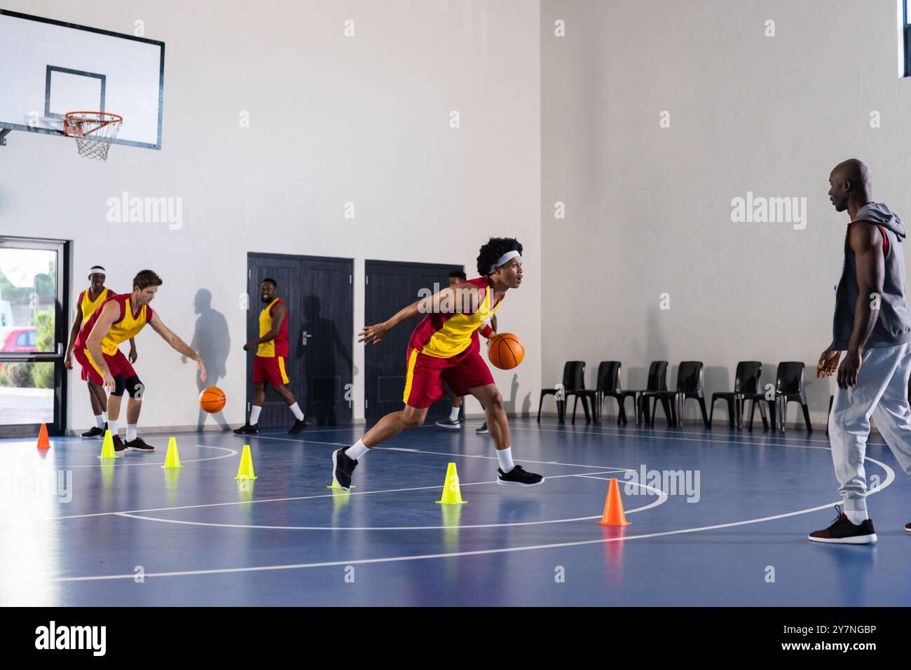 Practicing basketball drills, players dribbling around cones in gym ...