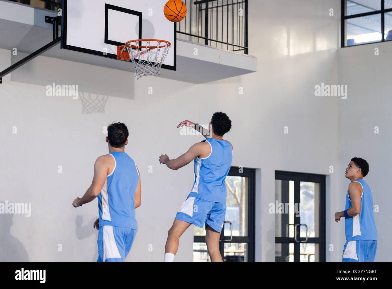 Playing basketball, three young men in blue uniforms shooting hoops ...