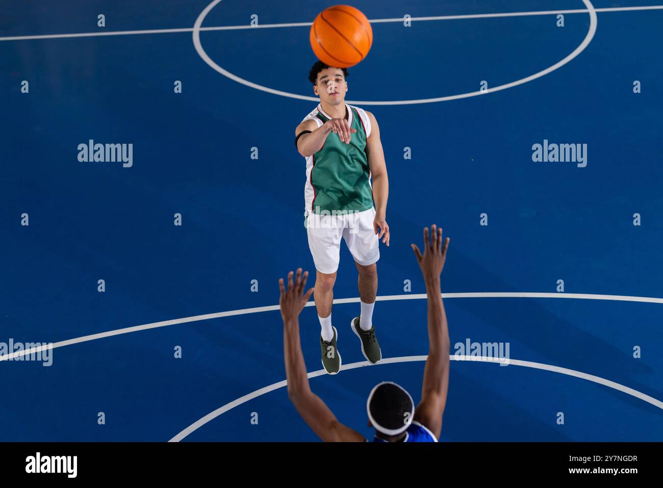 Playing basketball, athlete in green jersey shooting ball over defender ...