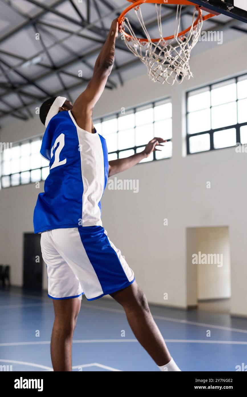 Playing basketball, athlete in blue jersey dunking ball in indoor court ...