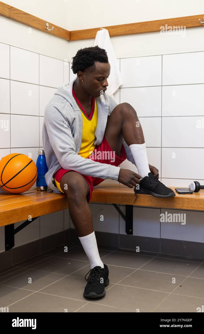 Tying shoelaces, basketball player sitting on bench in locker room with ...