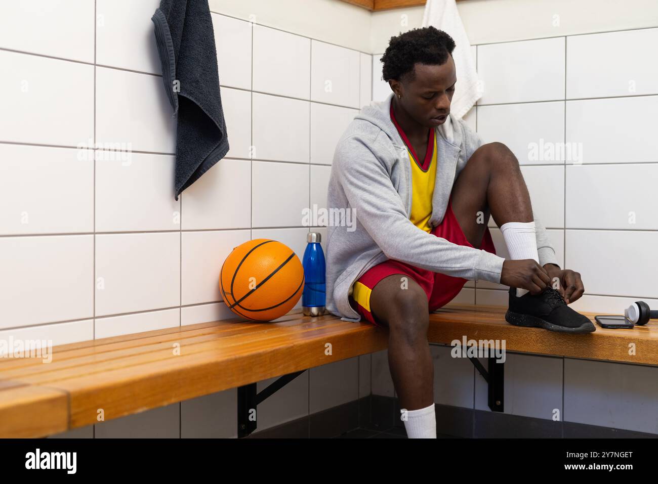Tying shoelaces, basketball player sitting on bench in locker room with ...