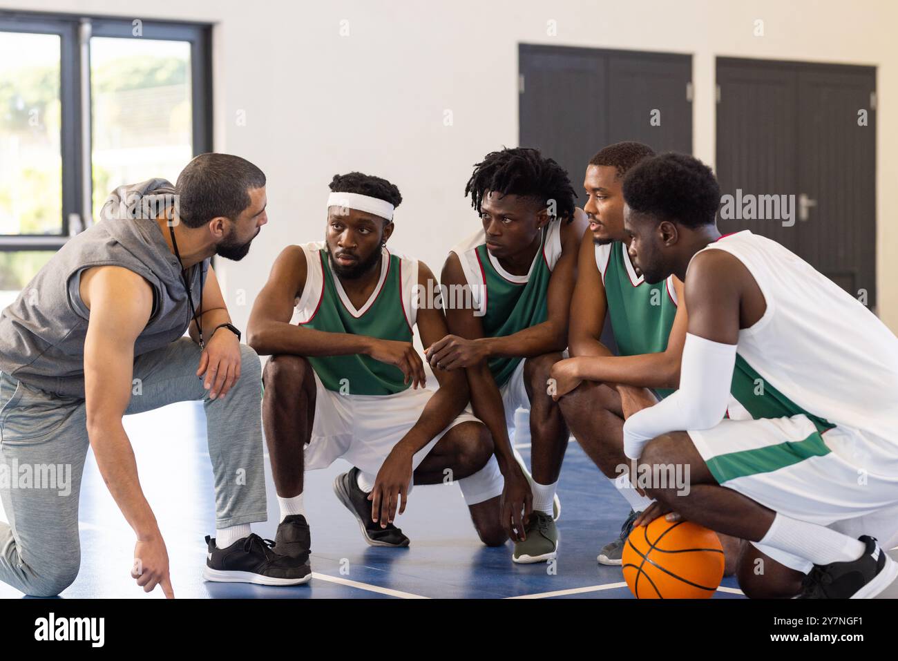 Basketball coach giving strategy to team players on court during ...