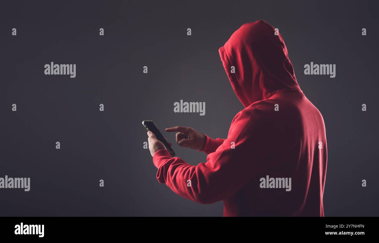 Man in a red hooded jacket, face fully concealed, uses a smartphone ...