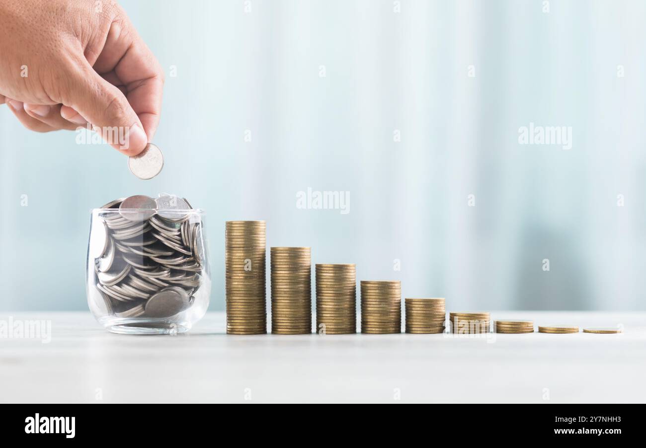 Hand drops coins into a glass jar, with stacks of coins arranged from ...