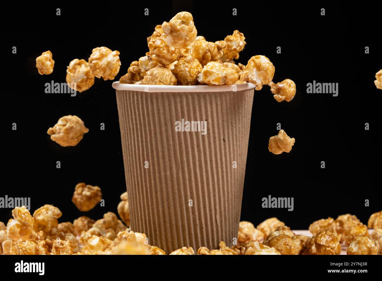 Sweet caramelized popcorn pouring into a glass on a black background ...