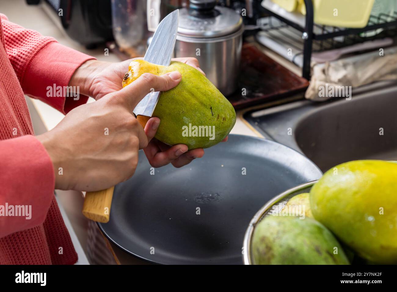 woman peeling ripe and juicy mango fruit with a sharp knife in the ...