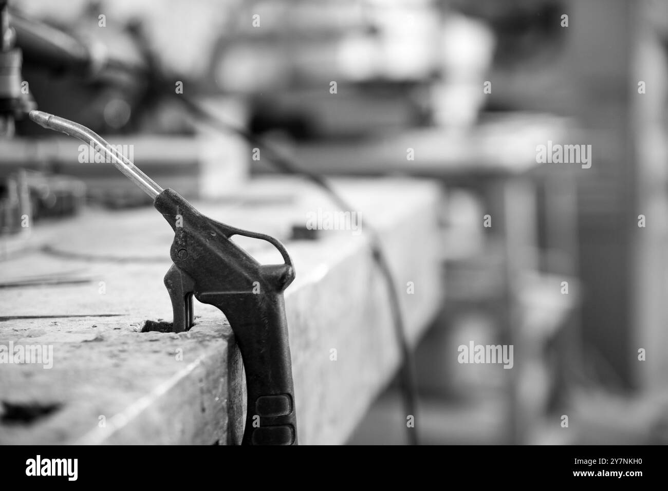 Black and white image of An air blow gun is resting on a workbench in a ...