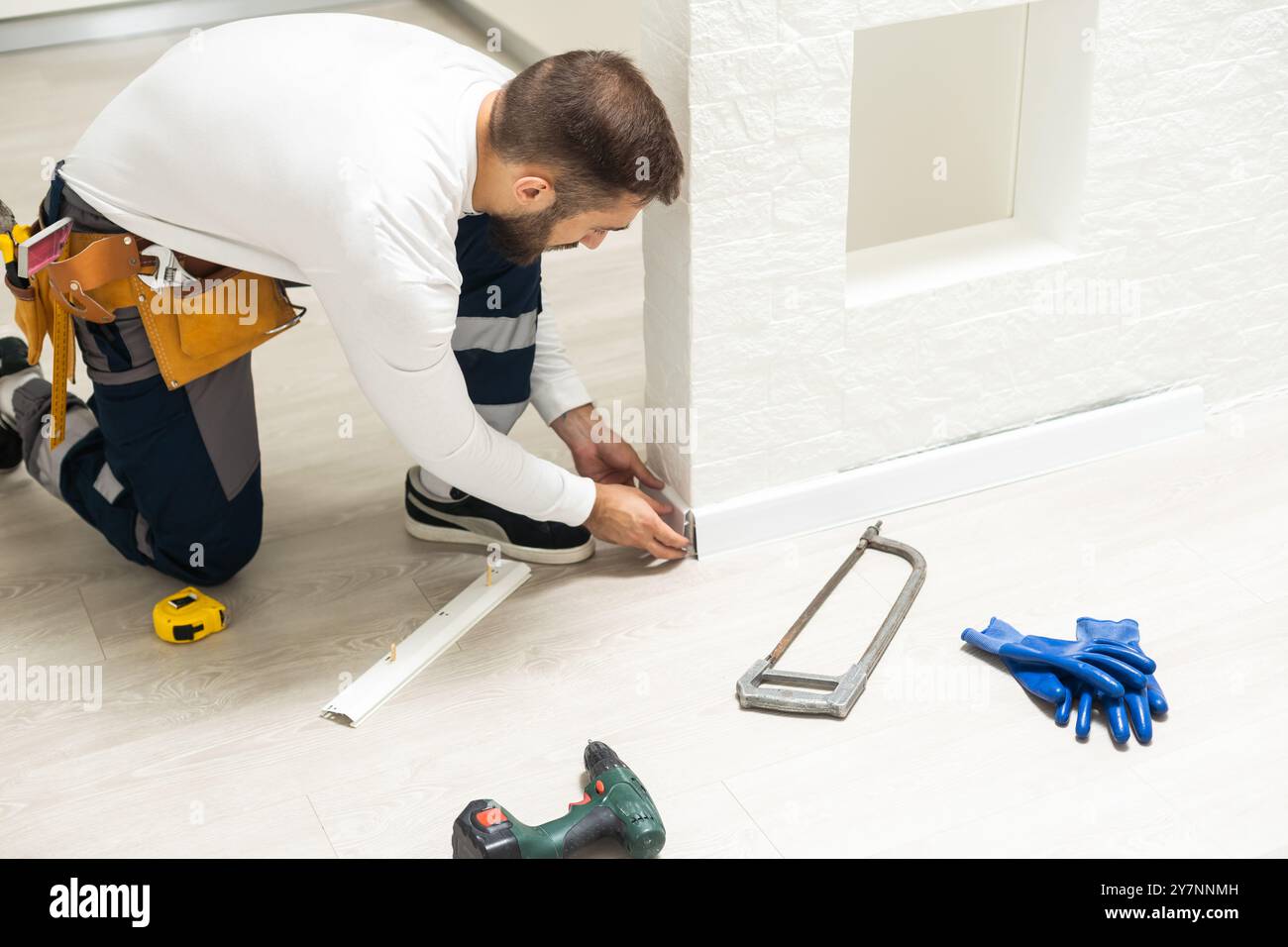A man installs a floor skirting board. Fixing the plastic skirting ...