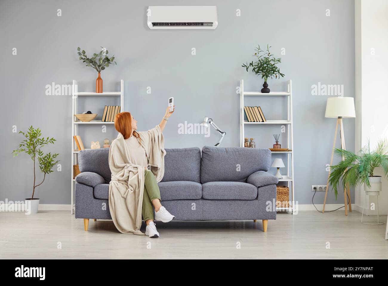 Girl wrapped in blanket switching on, off air conditioner, blowing warm ...