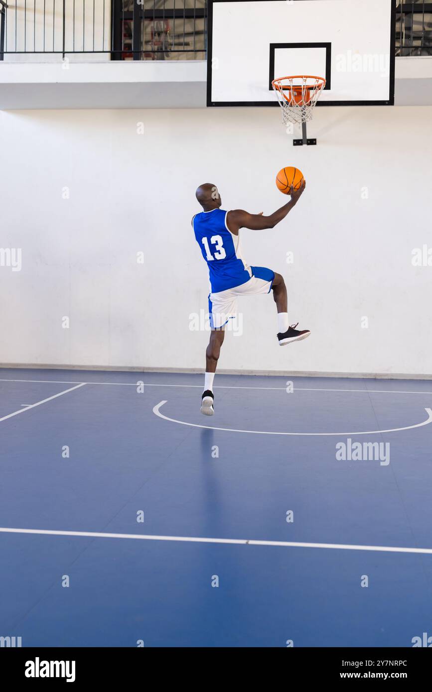Playing basketball, athlete in blue jersey making layup on indoor court ...