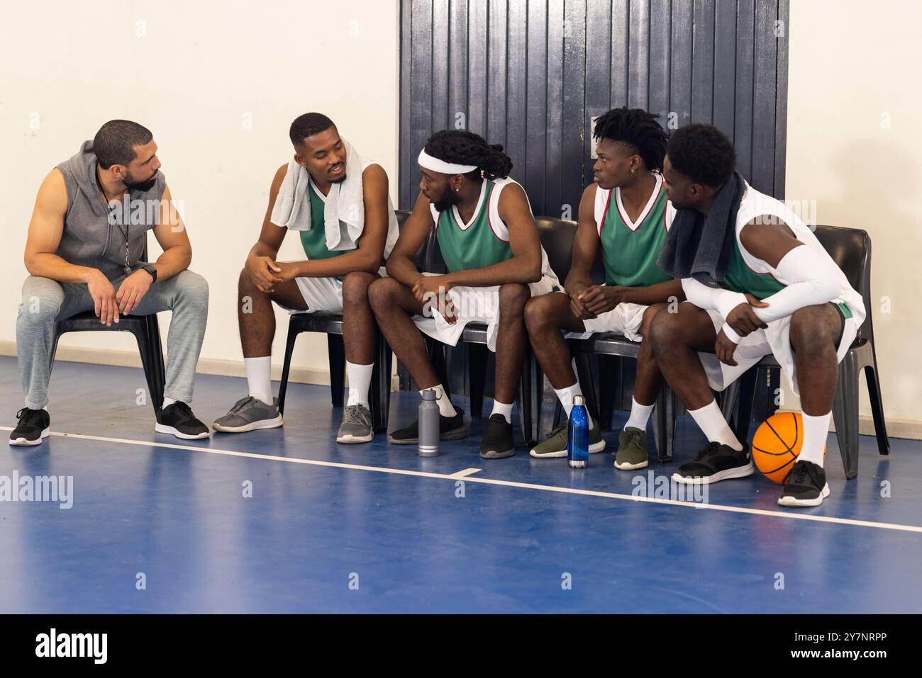African American basketball players sitting on bench talking with coach ...