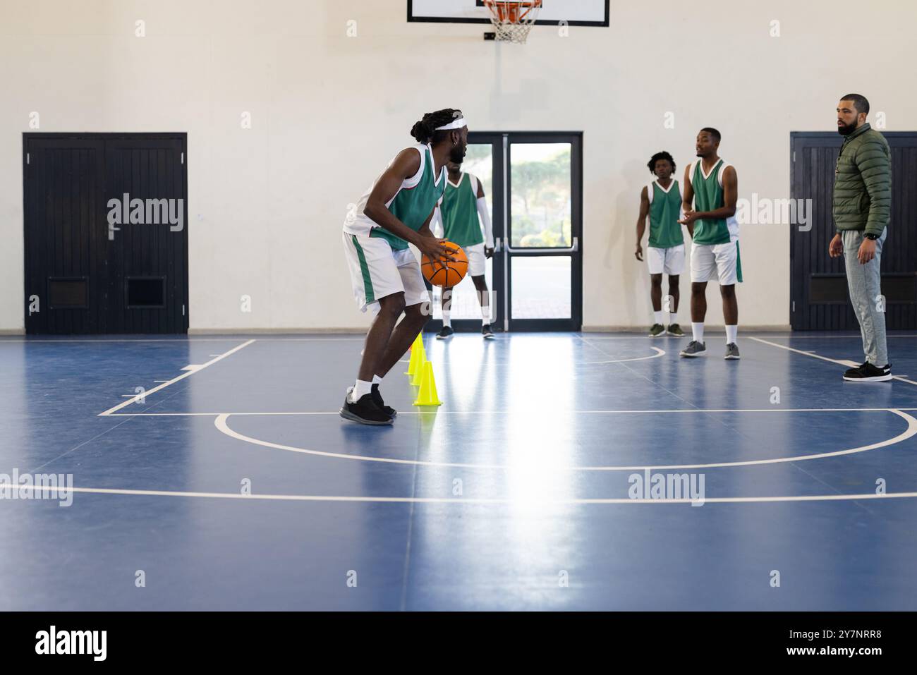 Practicing basketball, player dribbling ball around cones in school ...