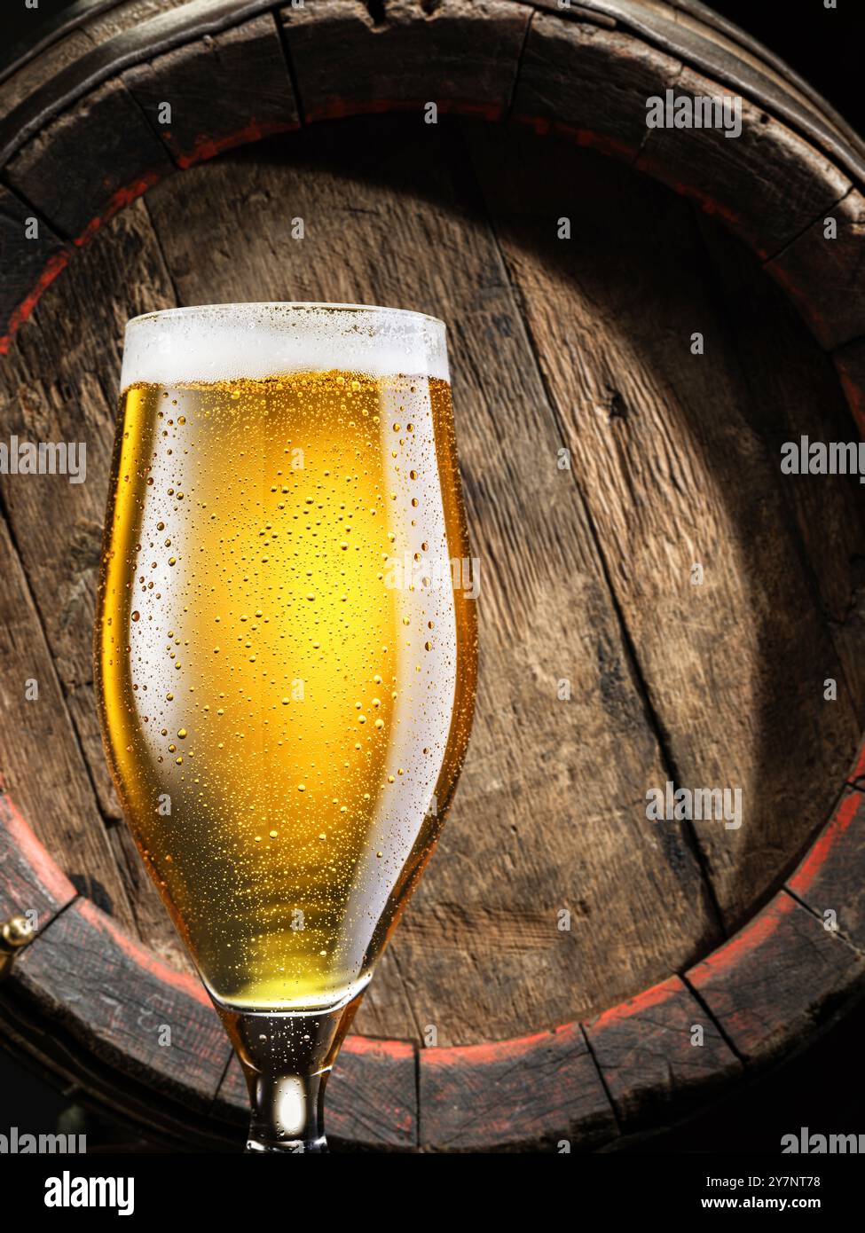Glass goblet of chilled beer and wooden beer cask on the background ...