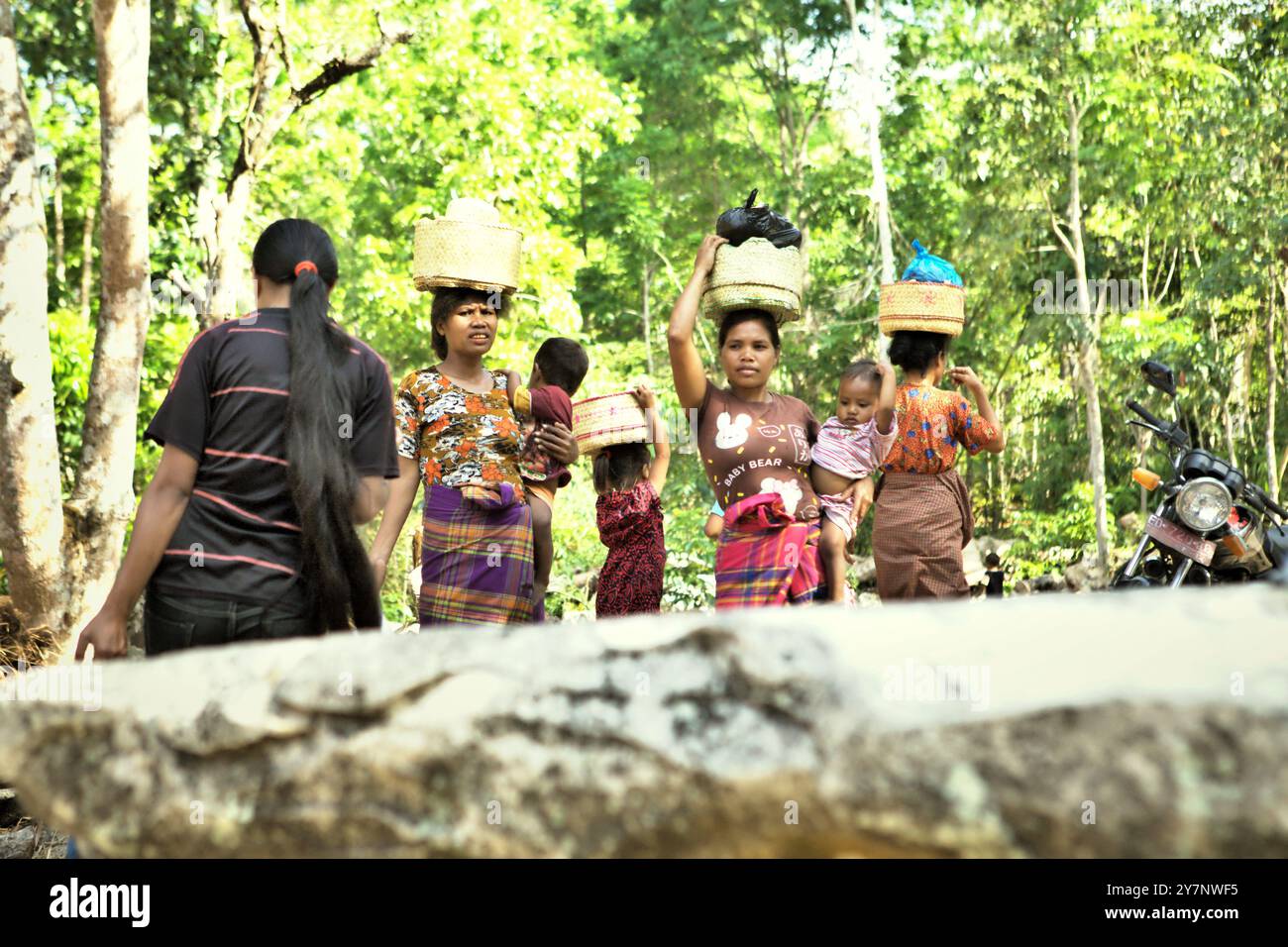 Women carry children by hands while bringing food materials on their ...