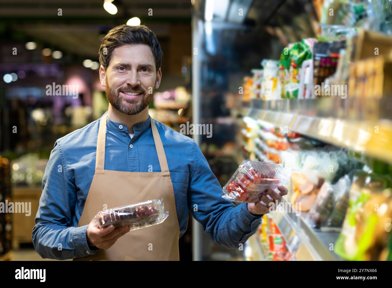 Smiling grocery store employee holding fresh produce in a supermarket ...