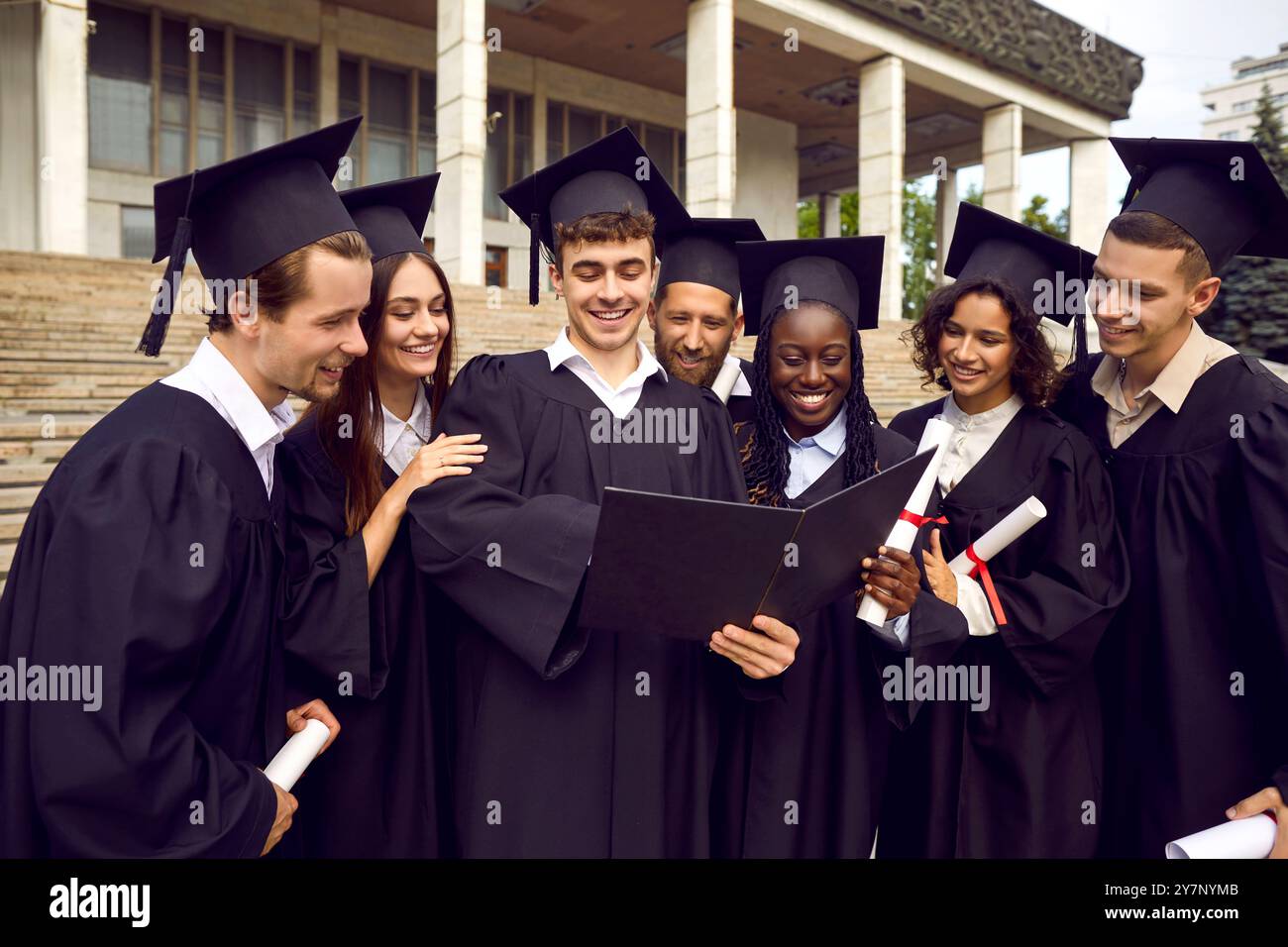 Group of happy multiracial university graduates look at their diploma ...