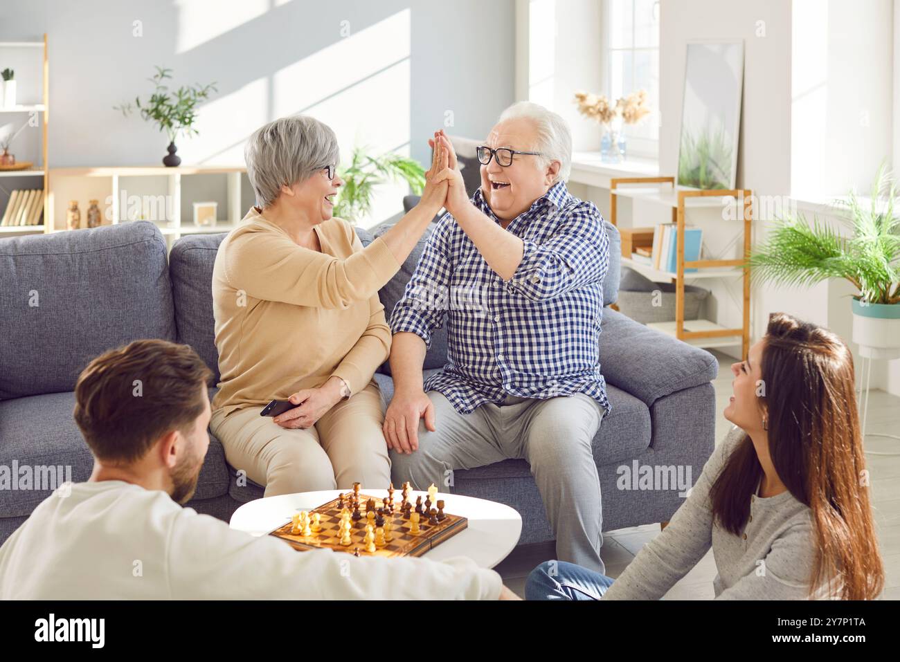 Happy senior old parents giving high five playing chess with adult ...