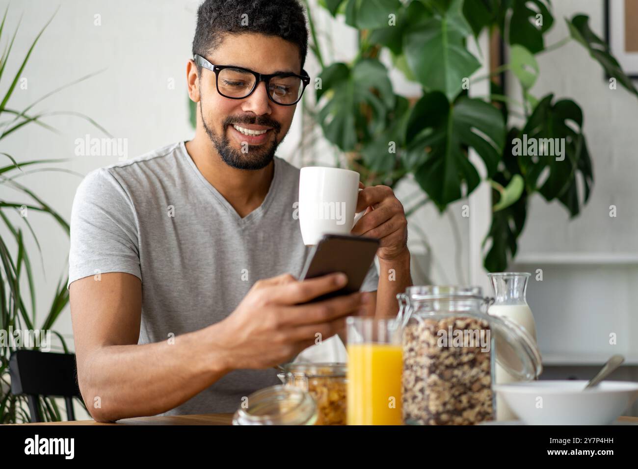 Happy black man using mobile phone while eating breakfast. People ...