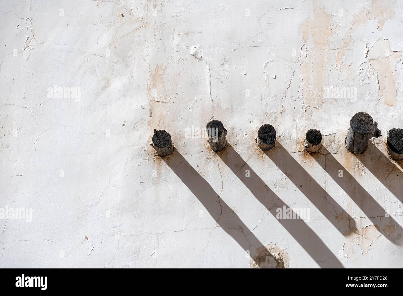 A white wall with wooden posts sticking out. The posts cast long ...