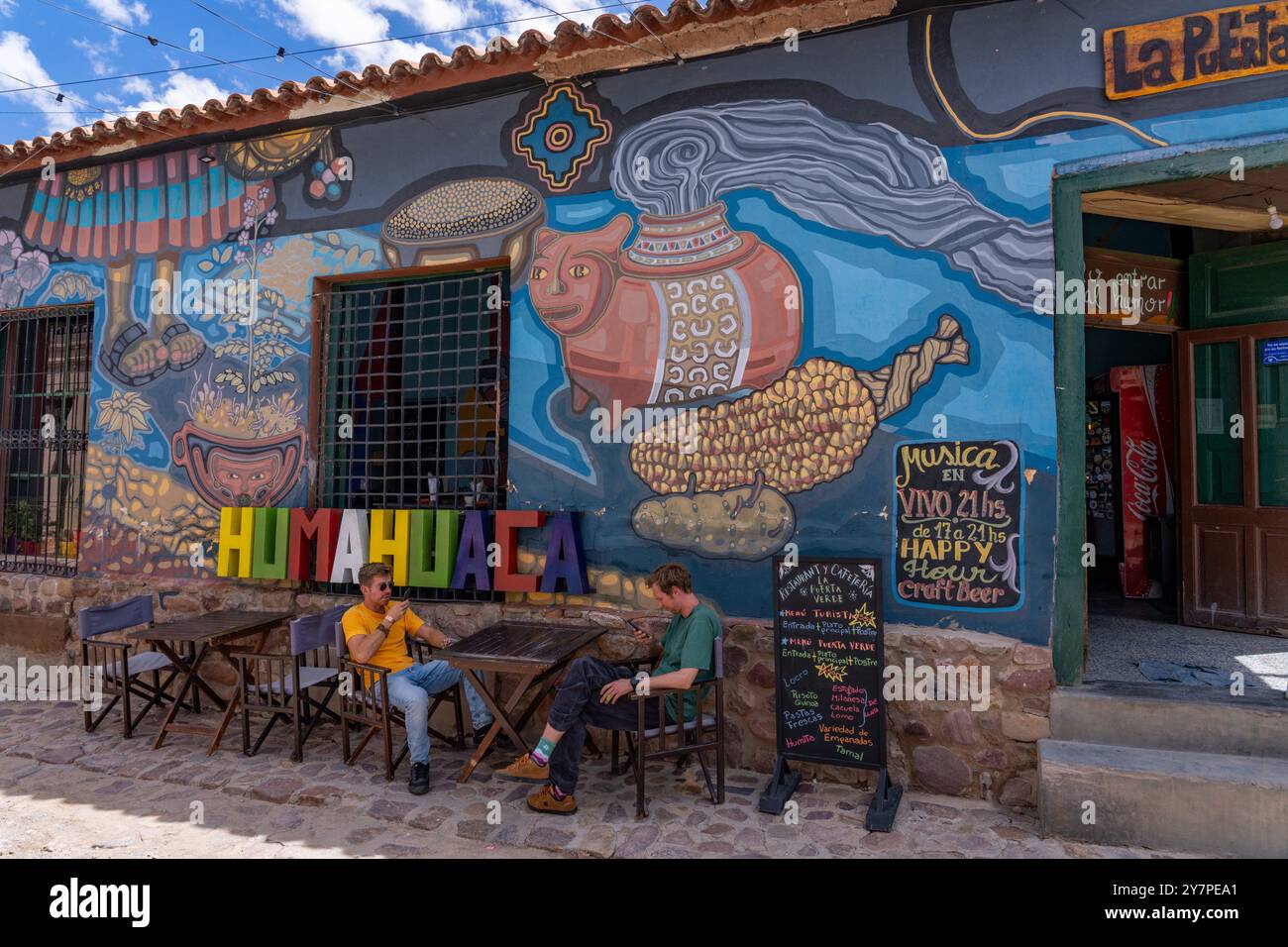 Tourists sit in front of a colorful mural on a restaurant in Humahuaca ...