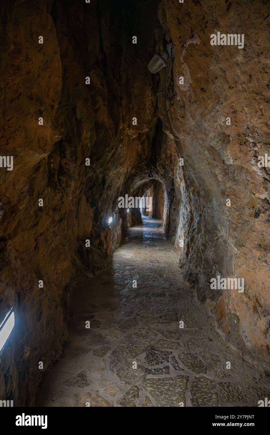 A narrow cave tunnel illuminated by small lights along the stone ...