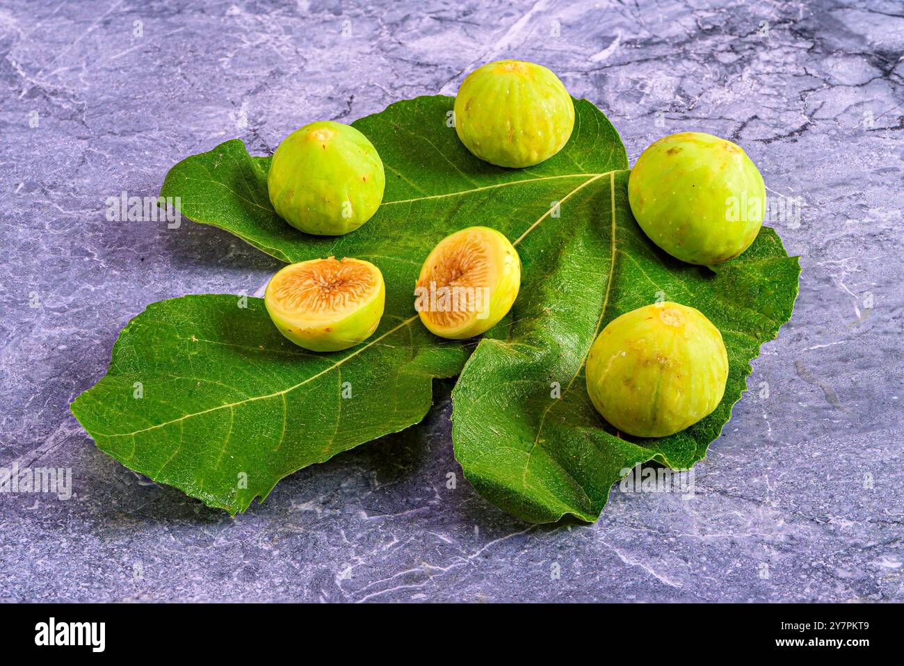Fresh green figs on fig leaves placed on a grey marble background ...